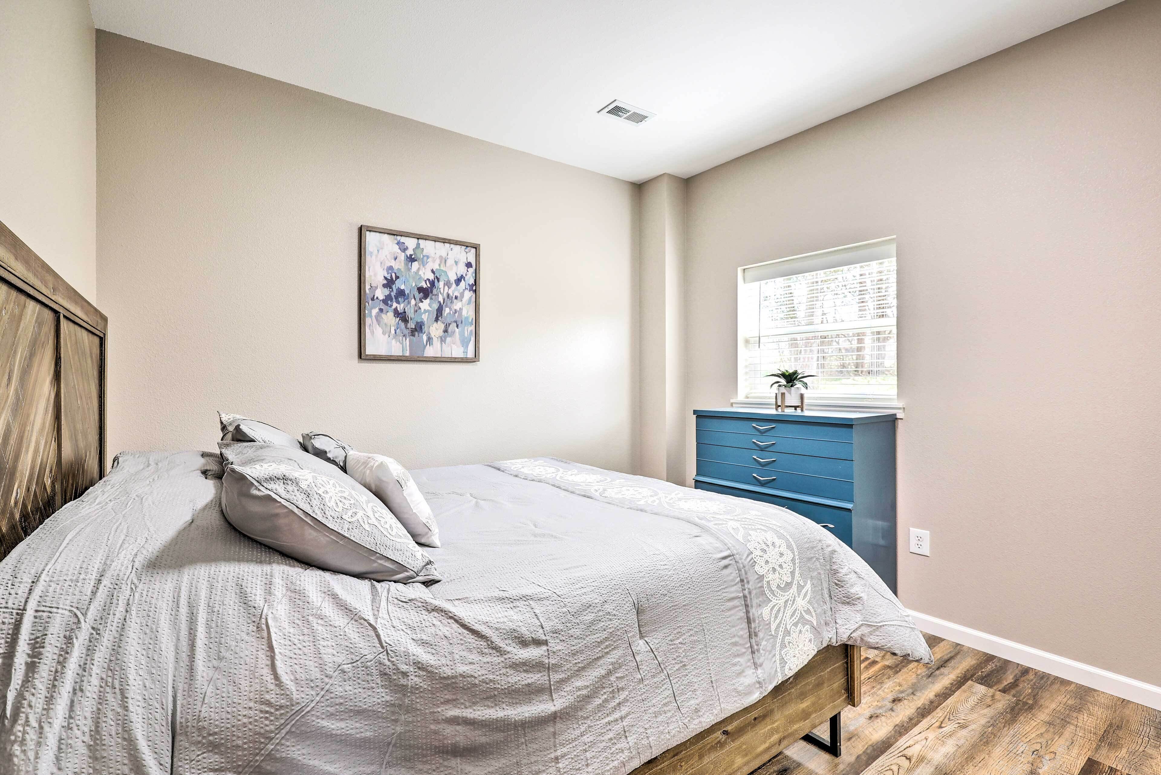 Um quarto com uma cama, cômoda, janela e um quadro na parede.