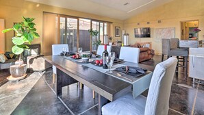 Uma sala de estar moderna com área de jantar, apresentando uma mesa comprida posta para refeição, assentos confortáveis e uma grande janela que proporciona iluminação natural.