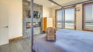 Quarto com cama, parede de pedra, televisão e vista para o oceano.