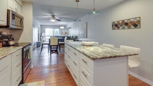 Uma cozinha moderna com armários brancos, bancada de mármore e iluminação pendente.