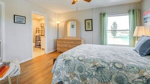 Quarto com cama, ventoinha no teto, cômoda, espelho e janela com cortinas.
