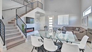 Uma sala de estar espaçosa com uma mesa de jantar de vidro, cadeiras brancas, um sofá seccional marrom e uma escada com corrimãos pretos.
