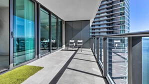 Uma varanda moderna com portas de vidro, um pequeno espaço de estar e vista para um edifício alto.