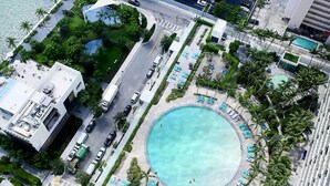 Vista aérea de um hotel com uma grande piscina circular rodeada por espreguiçadeiras e palmeiras.