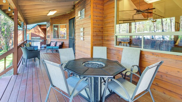 Uma cabana de madeira com um deck coberto, uma mesa de fogueira central e uma área de refeições.