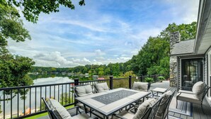 Um terraço com móveis de exterior, vista para um lago e um muro de pedra.