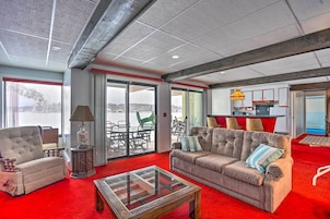 Uma sala de estar espaçosa com carpete vermelho, um sofá grande, uma mesa de centro e vista para uma área externa nevada através de uma porta de vidro.