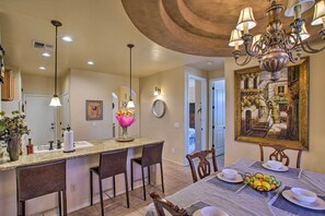 Cozinha com ilha central, banquetas, mesa de jantar para quatro e lustre.