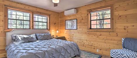 Quarto com cama, poltrona, ventoinha no teto e grandes janelas.
