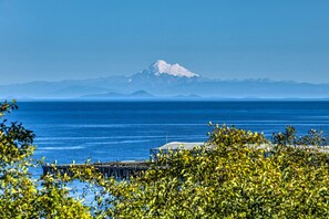 Vista costeira com uma montanha ao fundo, um cais e vegetação em primeiro plano.