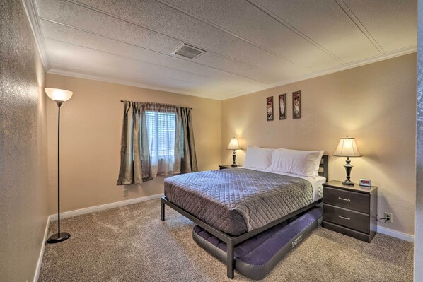 Quarto com cama, mesas de cabeceira, luminária e janela com cortinas.