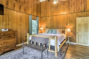Quarto com painéis de madeira, uma cama, abajures, cômoda e um banquinho.