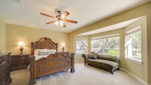 Quarto com uma cama grande, duas luminárias de cabeceira, um ventilador de teto e vista para o exterior através de amplas janelas.