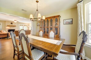 Uma sala de jantar com uma mesa e cadeiras de madeira, um candelabro e um armário grande de madeira com portas de vidro.