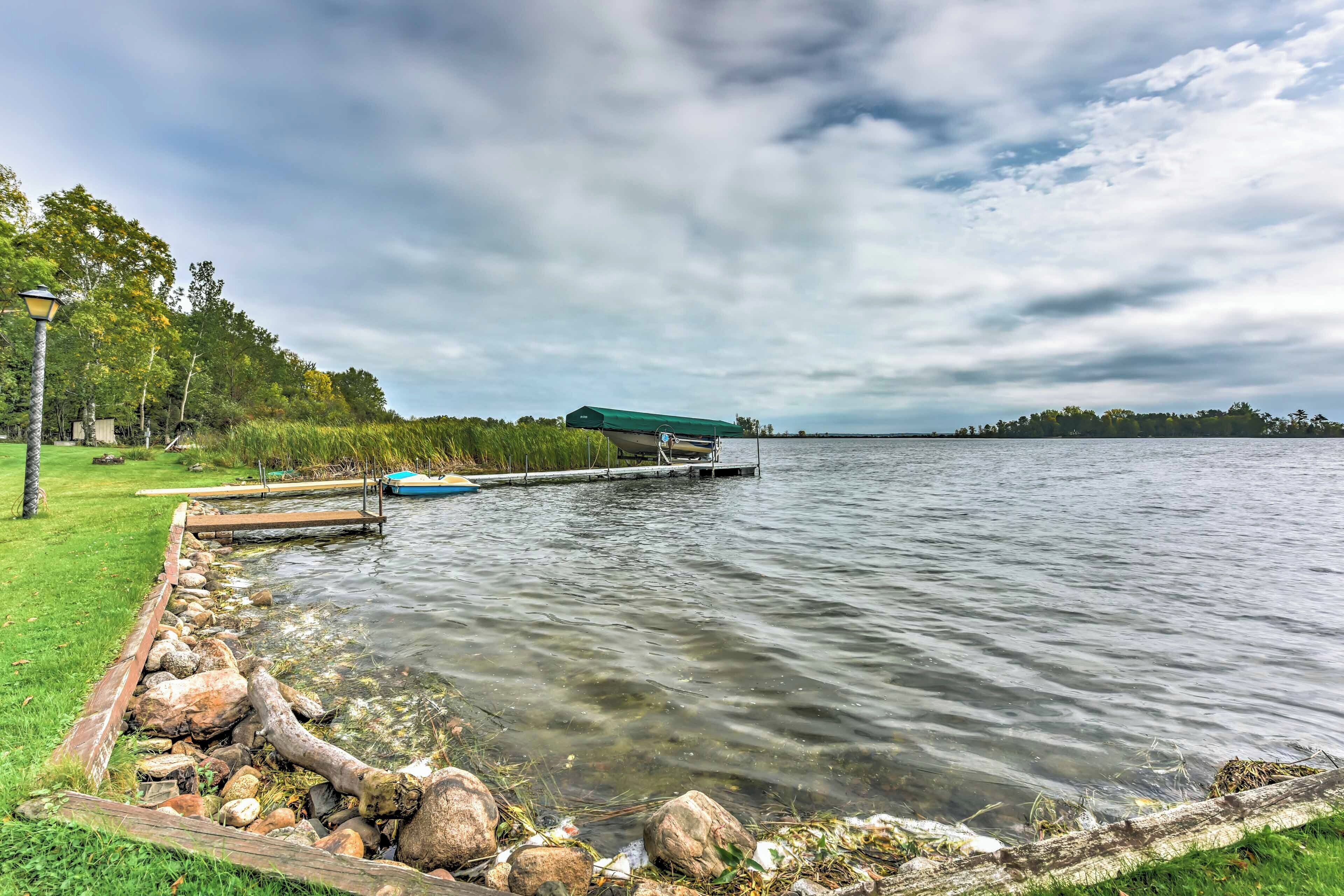 Um lago tranquilo com um cais, um barco coberto e uma área gramada com um poste de luz.