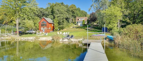 Uma propriedade à beira do lago com um píer, um edifício vermelho e uma casa rodeada por árvores.