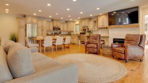 Uma cozinha moderna com eletrodomésticos embutidos, uma sala de jantar com mesa e cadeiras, e uma sala de estar com sofá e poltronas de couro.