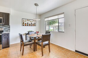 Área de refeições com mesa e cadeiras, cozinha com armários escuros e janela com vista para áreas verdes.