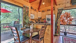 Interior de uma cabana de madeira com cozinha, sala de jantar e grandes janelas.