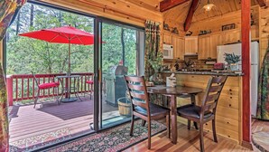 Uma cabana de madeira com varanda, área de refeições com cadeiras e mesa, e cozinha equipada.