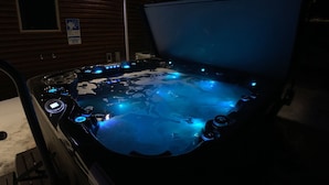 Uma banheira de hidromassagem com jatos iluminados, instalada em uma cabana de madeira com janela e uma placa na parede.