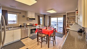 Cozinha moderna com eletrodomésticos de aço inoxidável, mesa de jantar posta para quatro pessoas e grandes janelas com vista para o exterior.