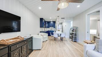 Uma sala de estar moderna com televisão de tela plana, um ventilador de teto e um espaço de jantar com mesa e cadeiras.
