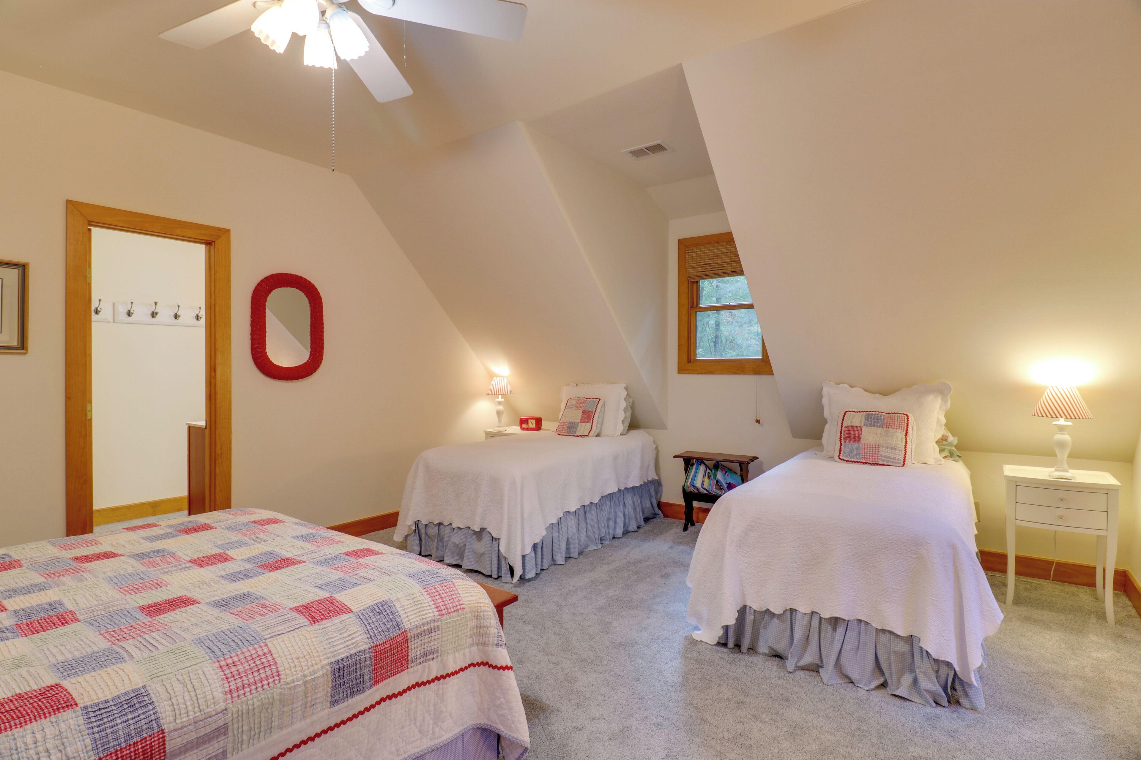 Quarto com duas camas, um ventilador de teto, uma janela e uma porta com ganchos.