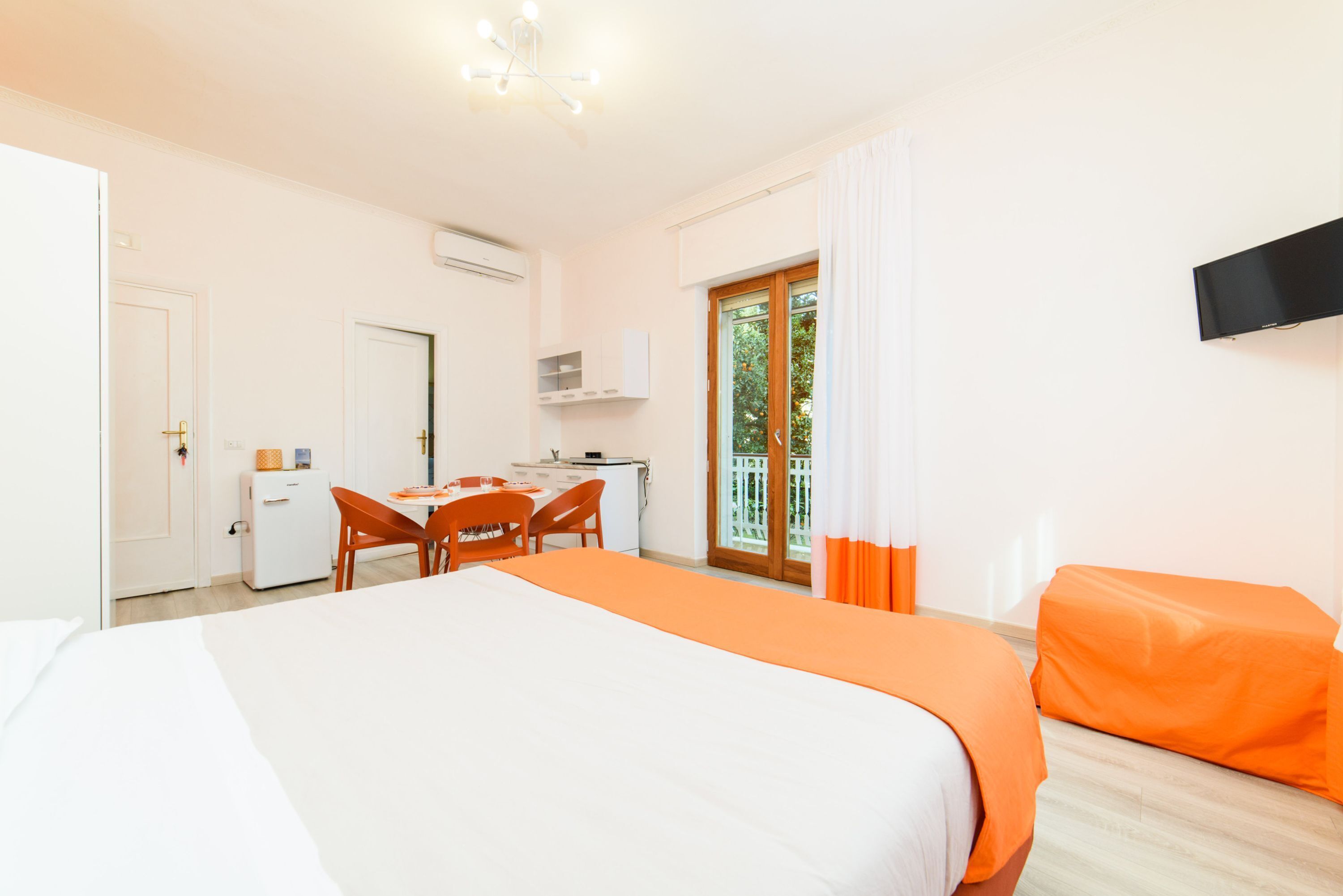 Quarto de hotel com cama, escrivaninha, cadeira e televisão.