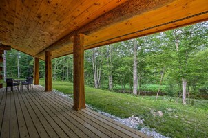 Um deck de madeira com mesa e cadeiras, com vista para uma área arborizada e um riacho.