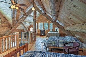 Quarto de sótão acolhedor, com vigas de madeira, duas camas, uma escrivaninha e uma cadeira.