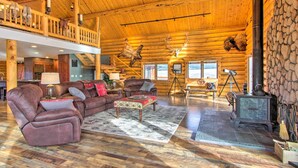 Interior espaçoso de uma cabana de toras, com um amplo sofá de couro, lareira e varanda com chifres de veado.