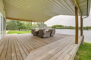 Um deck de madeira com móveis externos e vista para um lago.