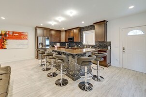 Uma cozinha moderna com uma ilha central, banquetas, eletrodomésticos de aço inoxidável e uma janela grande.