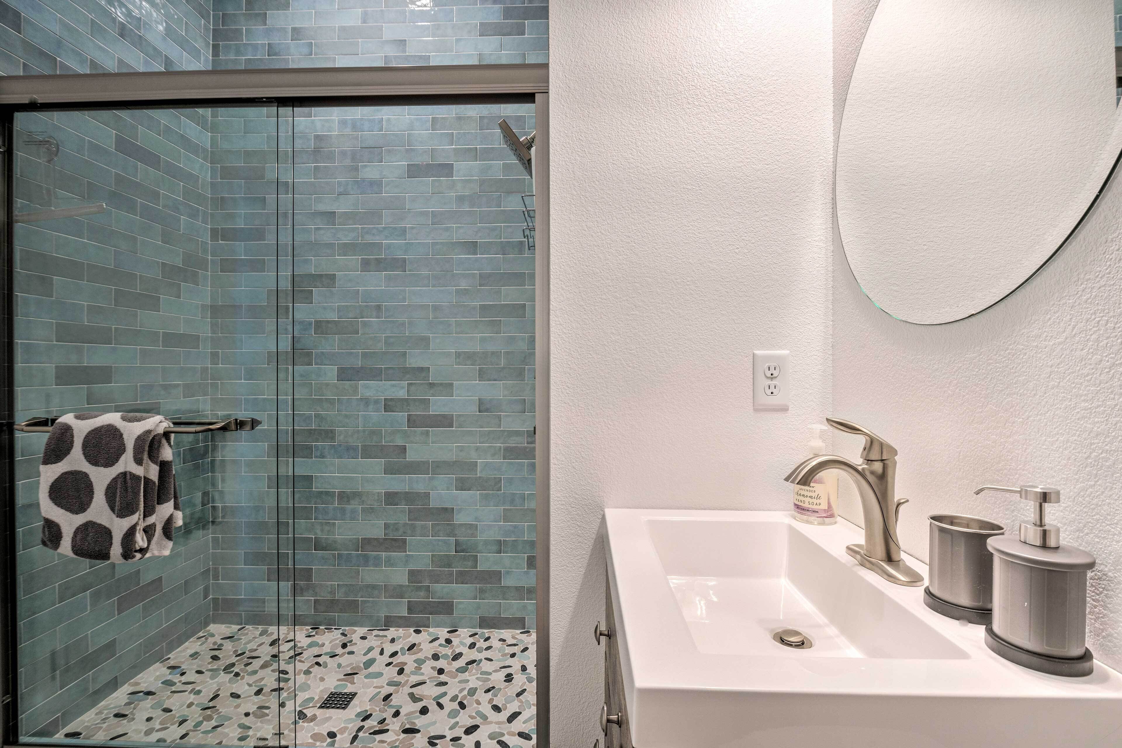 Casa de banho com cabine de duche em vidro, lavatório branco com torneira moderna e espelho redondo.