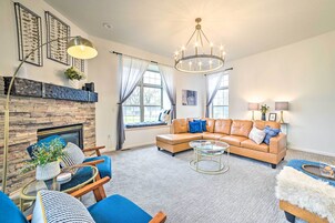 Uma sala de estar com lareira de pedra, sofá de couro, poltronas azuis e um candelabro.