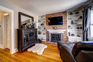 Uma sala de estar com lareira, uma televisão montada acima e um sofá de couro.
