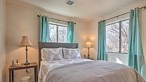 Quarto com cama, duas mesas de cabeceira, abajur e janela com cortinas.