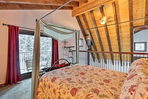 Quarto com teto de madeira, cama com roupa de cama floral, varanda com cortinas vermelhas e luminária pendente.