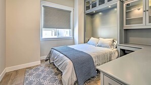 Quarto com cama, janela com persianas, armários embutidos e tapete estampado.