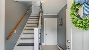 Uma escadaria com corrimãos de madeira e degraus brancos, que leva a uma porta branca com uma grinalda verde.
