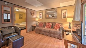 Sala de estar com sofá de couro marrom, um banquinho combinando e uma mesa de centro de madeira. Há um espelho na parede e um quadro emoldurado acima do sofá.