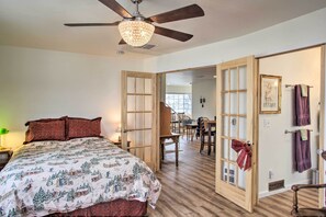Quarto com cama, ventilador de teto e porta que dá para uma sala de jantar.