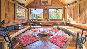 Interior rústico de cabana de madeira, com uma grande mesa de jantar, jogos americanos vermelhos e uma imagem de urso na parede.