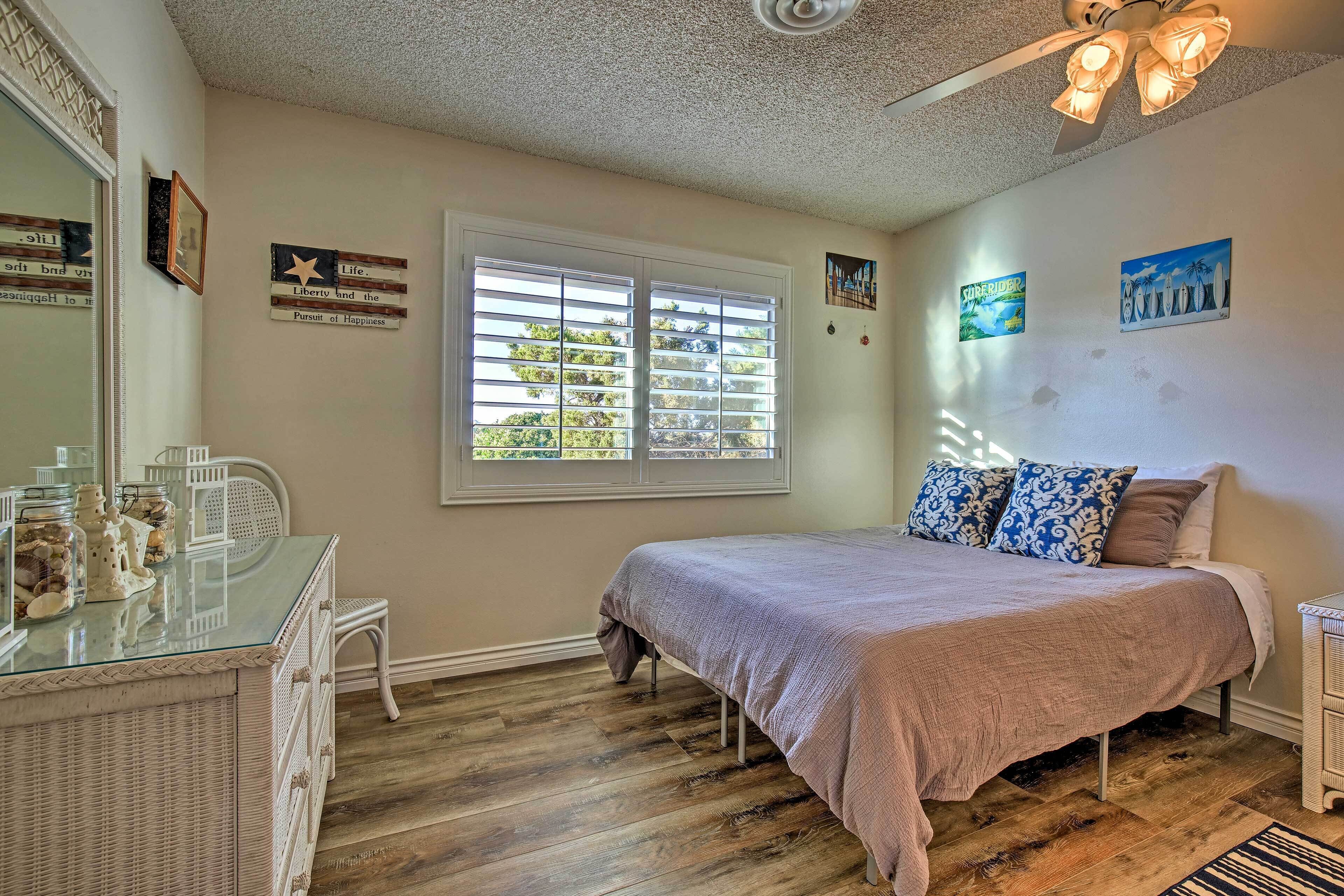 Quarto com cama, cômoda, janela com persianas e decoração nas paredes.