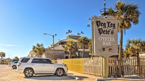 Placa do 'Peg Leg Pete's Oyster Bar' com cerca de madeira e palmeiras ao fundo.