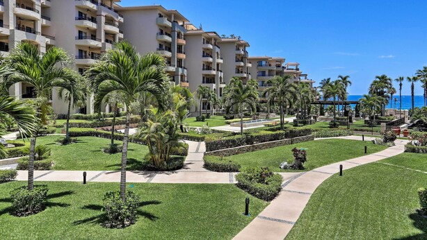 Um resort com edifícios de vários andares, palmeiras e um gramado bem cuidado.