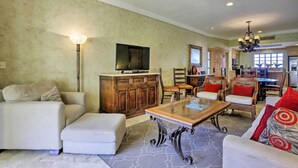 Uma sala de estar ampla com televisão de tela plana, armários de madeira, uma mesa de jantar e assentos confortáveis.