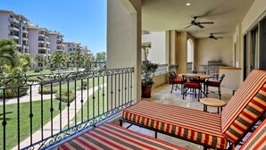 Uma varanda com almofadas listradas, um espaço de refeições com mesa e cadeiras, e vista para um edifício residencial.