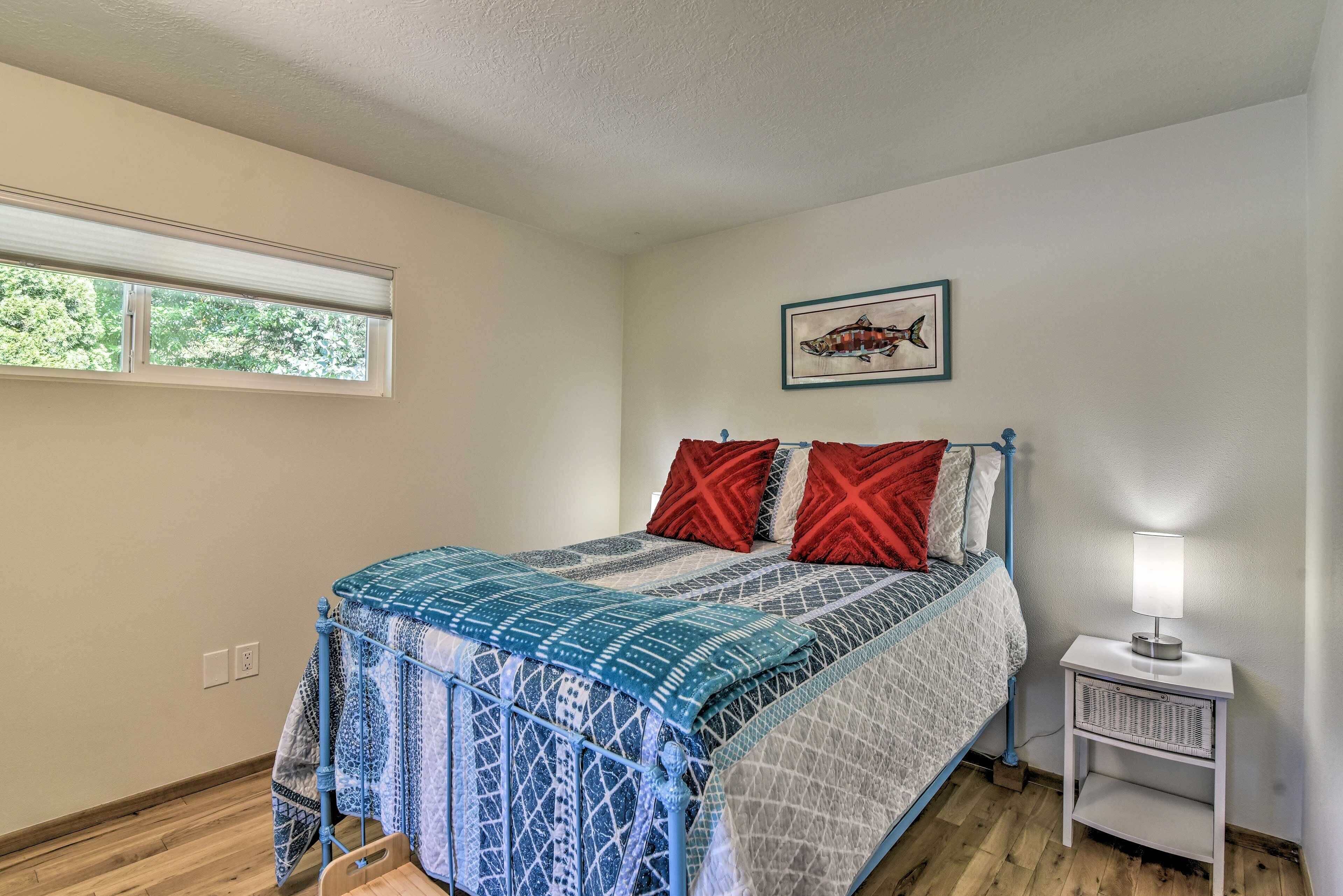 Quarto com cama, mesa de cabeceira, janela e um quadro de peixe na parede.
